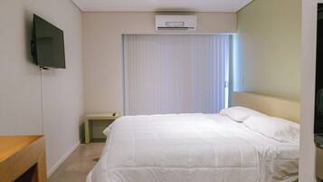 Quarto de hotel com cama, televisão presa à parede, mesa de cabeceira e ar condicionado.