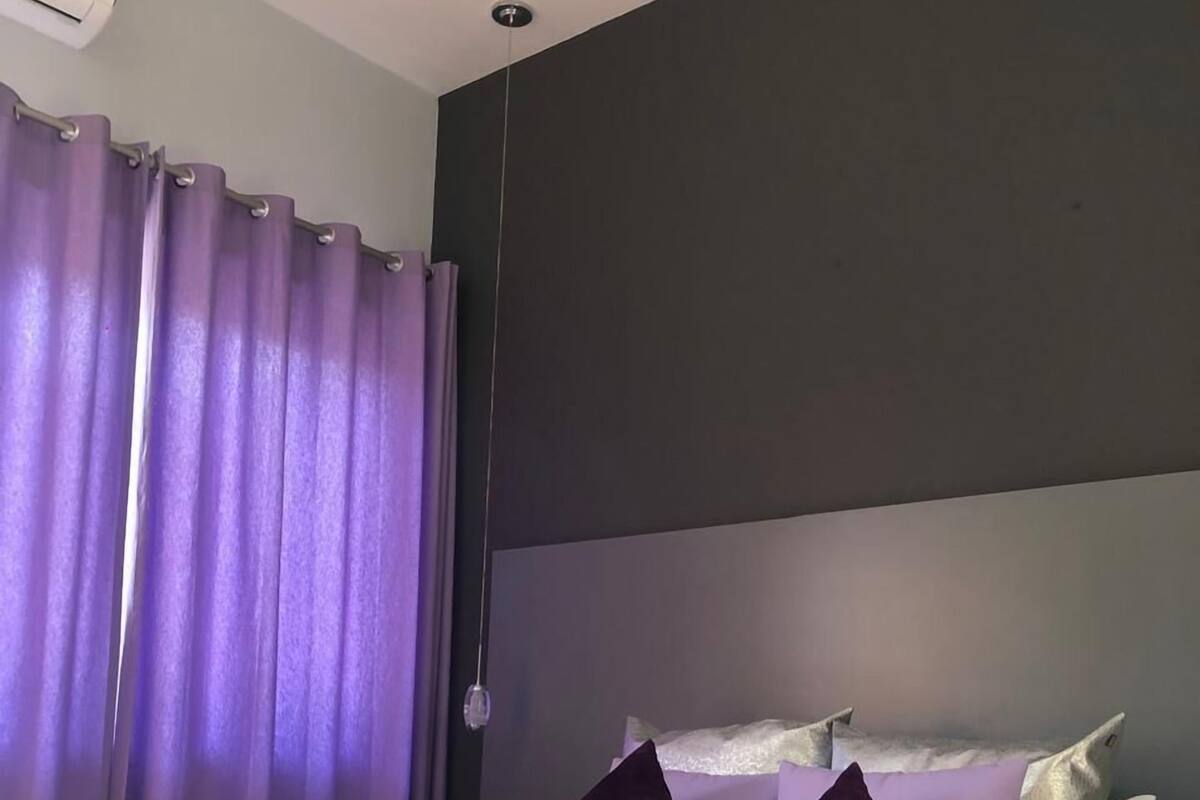 Quarto moderno com cama grande, roupa de cama roxa e parede de destaque escura.