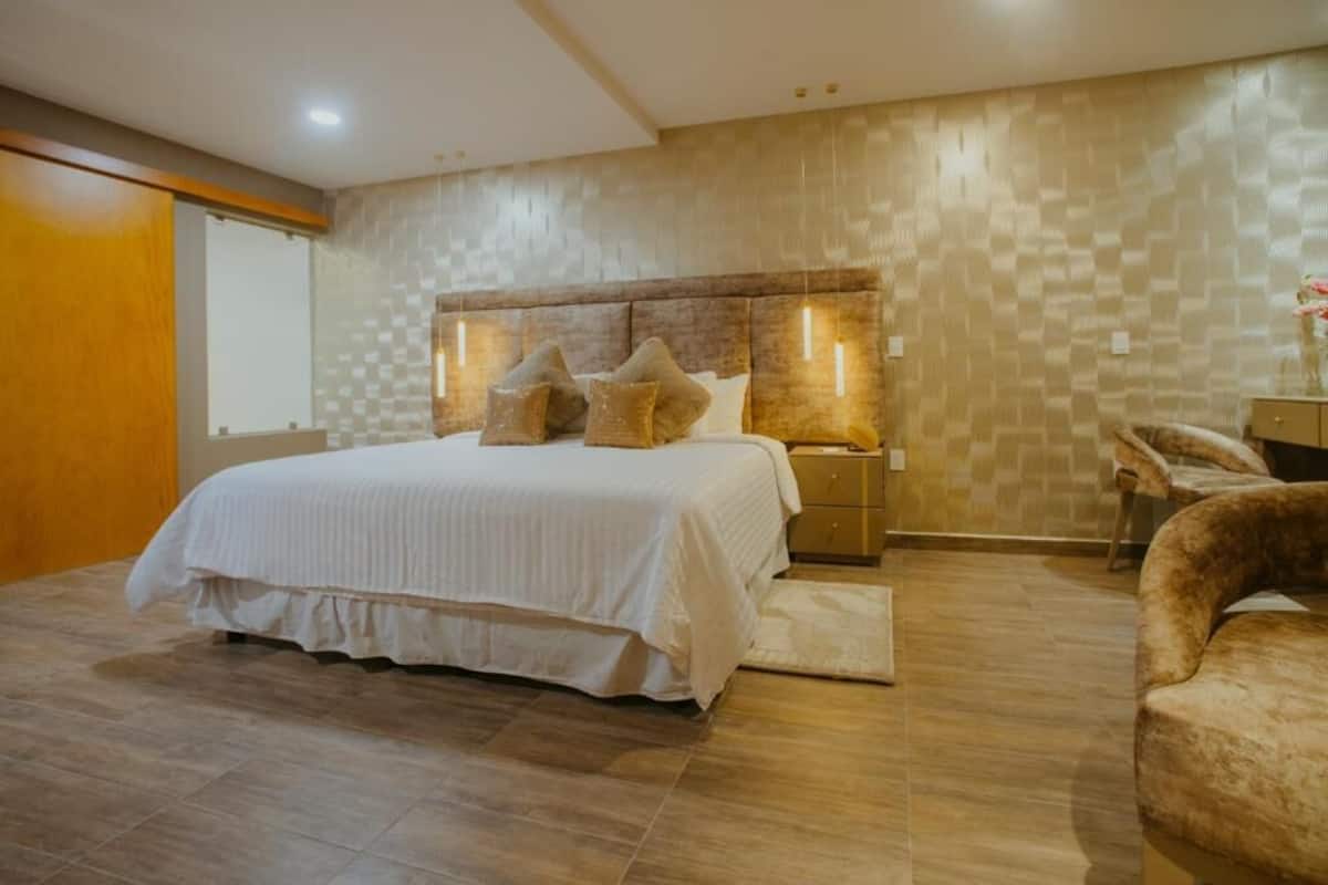 Quarto com uma cama grande, cabeceira de madeira, mesas de cabeceira e uma cadeira.