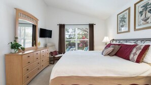 Quarto com uma cama grande, cómoda de madeira, televisão na parede e janela com cortinas.