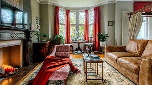Uma sala de estar aconchegante com lareira, um sofá de couro, uma poltrona rosa e um espaço de jantar com mesa e cadeiras.