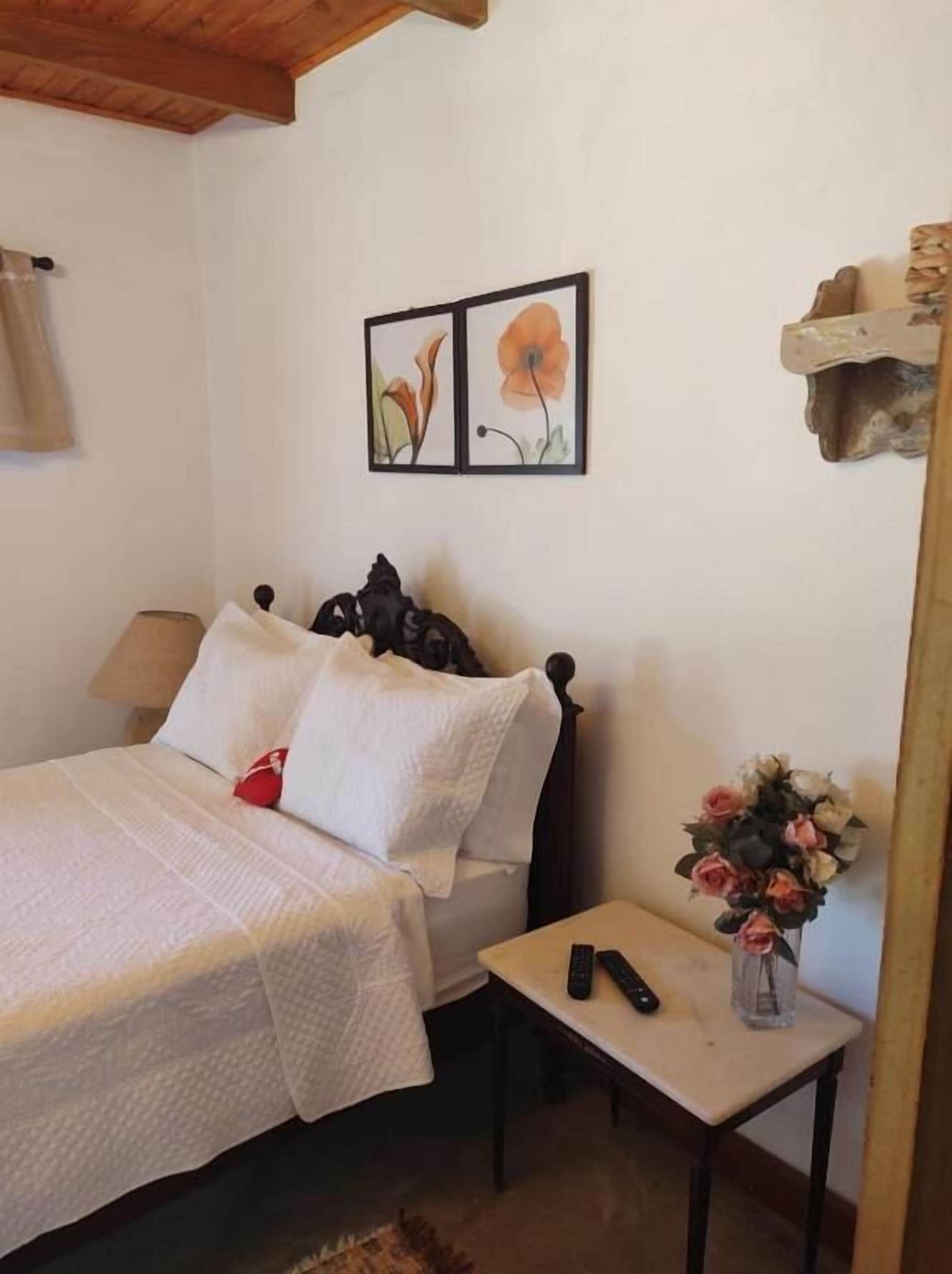 Um quarto com uma cama, uma mesa de cabeceira com um vaso de flores e dois quadros florais na parede.