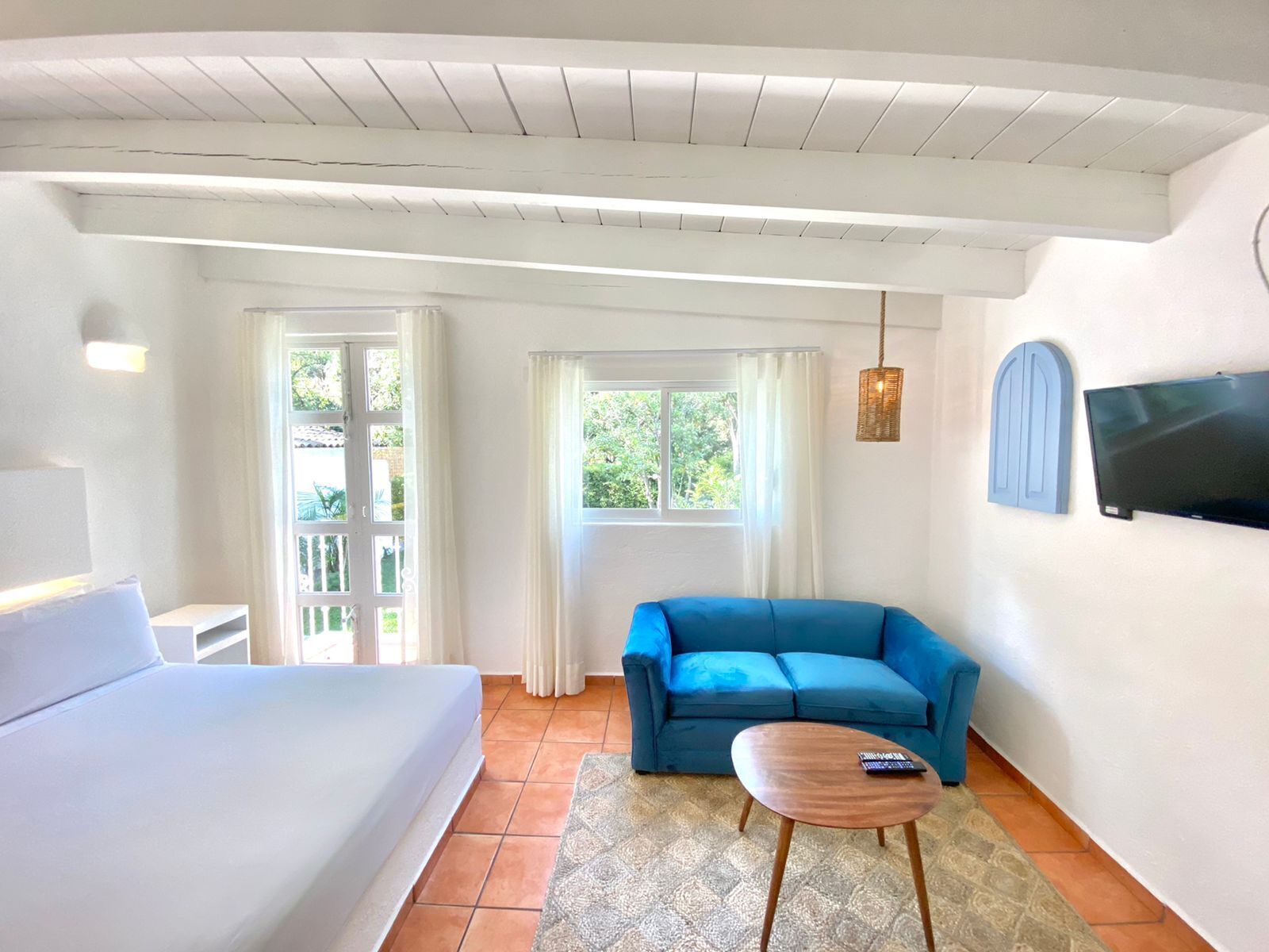 Quarto com cama, sofá azul, mesa pequena e televisão na parede.