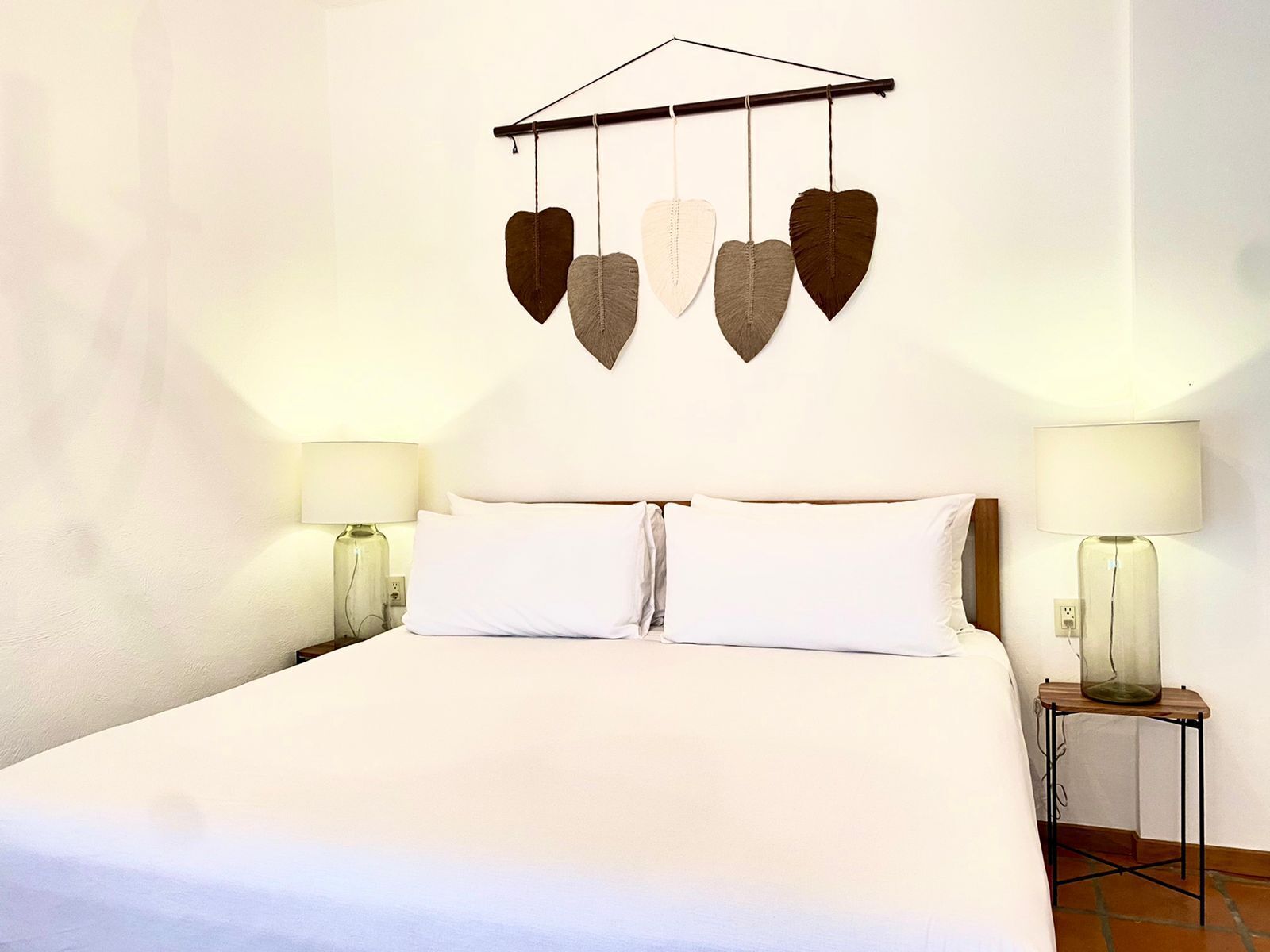 Quarto de hotel com uma cama grande, duas mesas de cabeceira com luminárias e uma luminária na parede com detalhes em formato de coração.