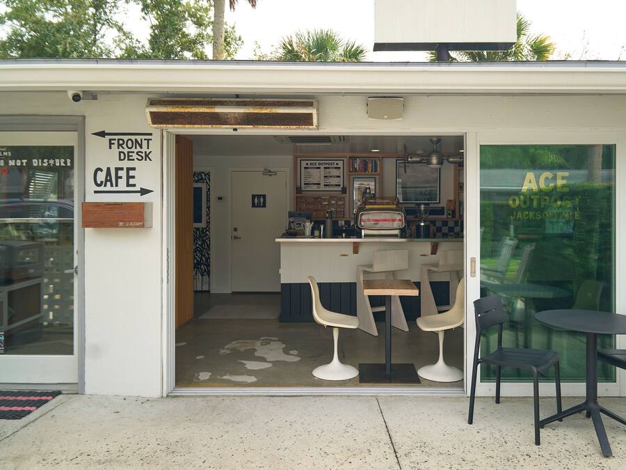 Café com balcão de atendimento, máquina de café e duas cadeiras na parte externa.