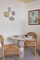 Quarto com uma mesa redonda de mármore, duas cadeiras de fibra e decorações na parede incluindo conchas e um quadro emoldurado.