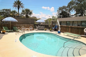 Piscina com deck de madeira, cadeiras de descanso e guarda-sóis.