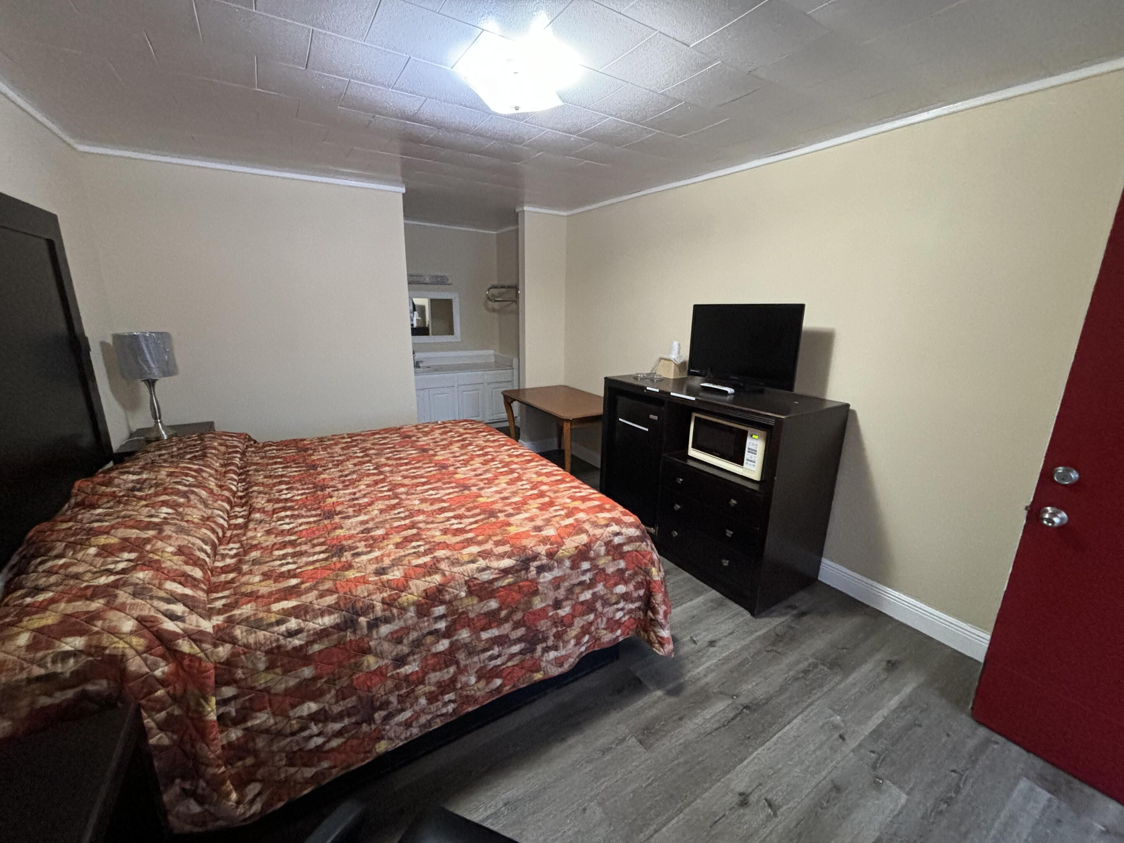 Quarto com cama, cômoda, televisão e banheiro visível por uma porta aberta.