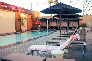 Uma área à beira da piscina com espreguiçadeiras e guarda-sóis, piscina e um restaurante chamado 'Aroma' ao fundo.