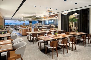 Um restaurante moderno com várias áreas de refeição, incluindo um bar e um espaço de estar com vista para a paisagem urbana.