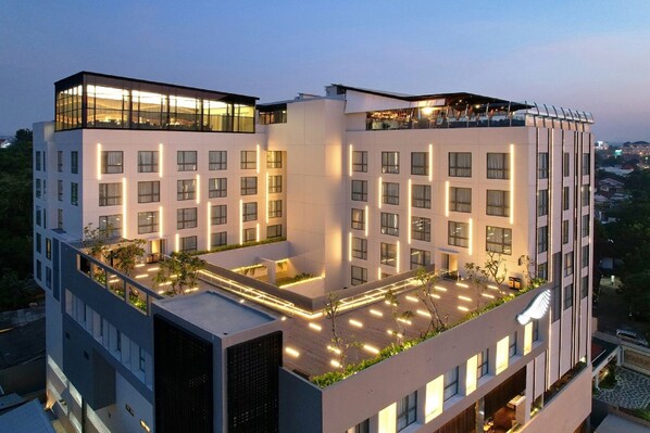 Um hotel moderno com vários andares, grandes janelas e um terraço no telhado com plantas.