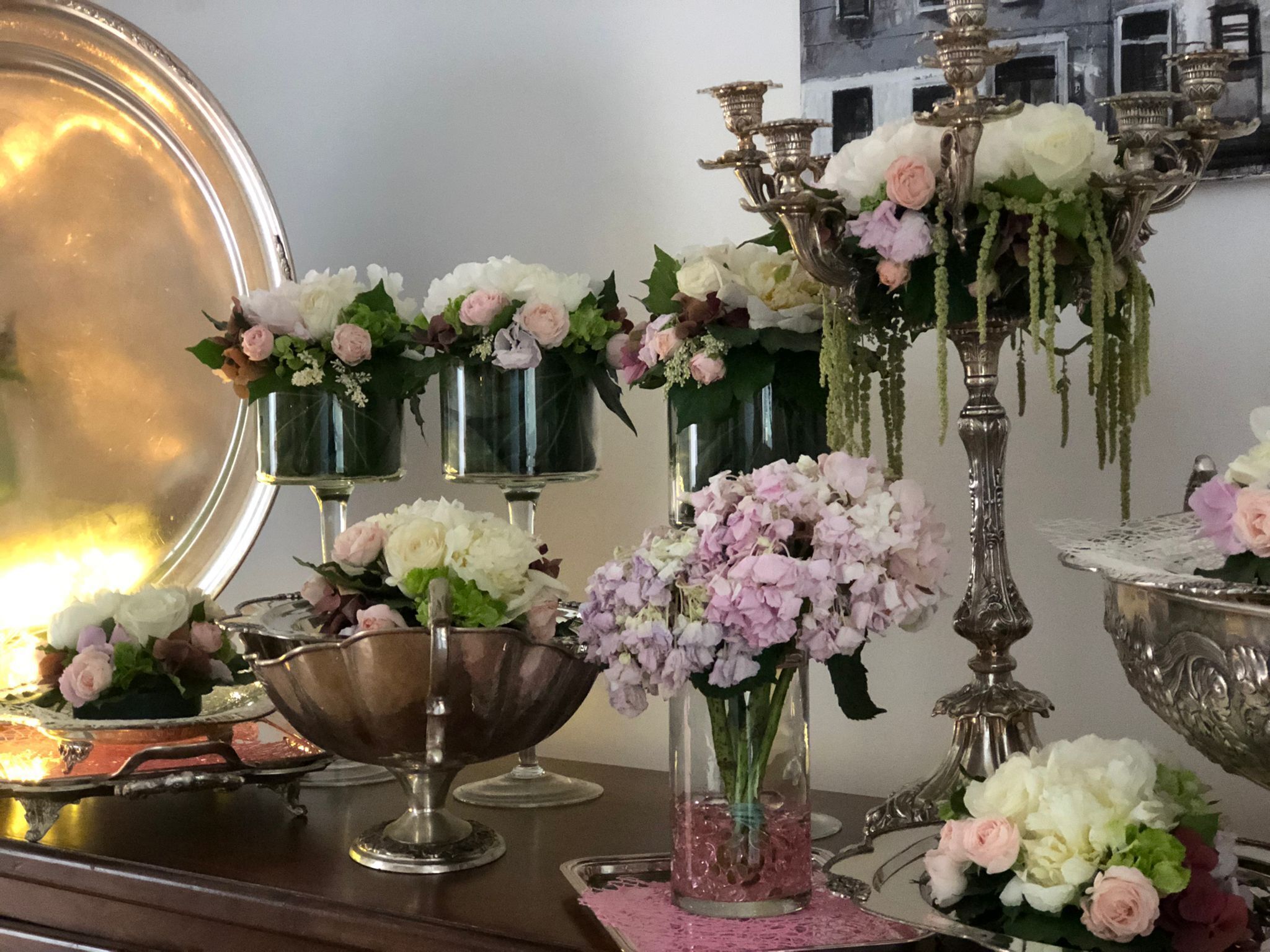 Uma mesa com arranjos florais diversos e candelabros de prata.