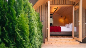 Uma cabana de madeira com uma cama, um cobertor vermelho e uma pequena escada que leva à entrada.