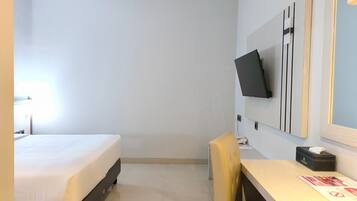 Quarto de hotel com cama, escrivaninha, cadeira, televisão fixada na parede e espelho.