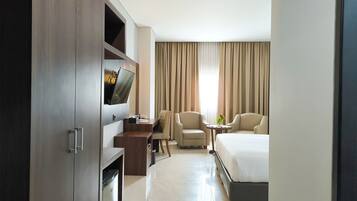 Quarto de hotel com cama, duas poltronas, escrivaninha com televisão e minibar.