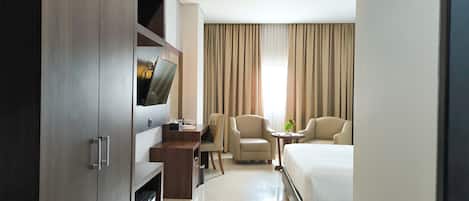 Quarto de hotel com cama, duas poltronas, escrivaninha com televisão e minibar.