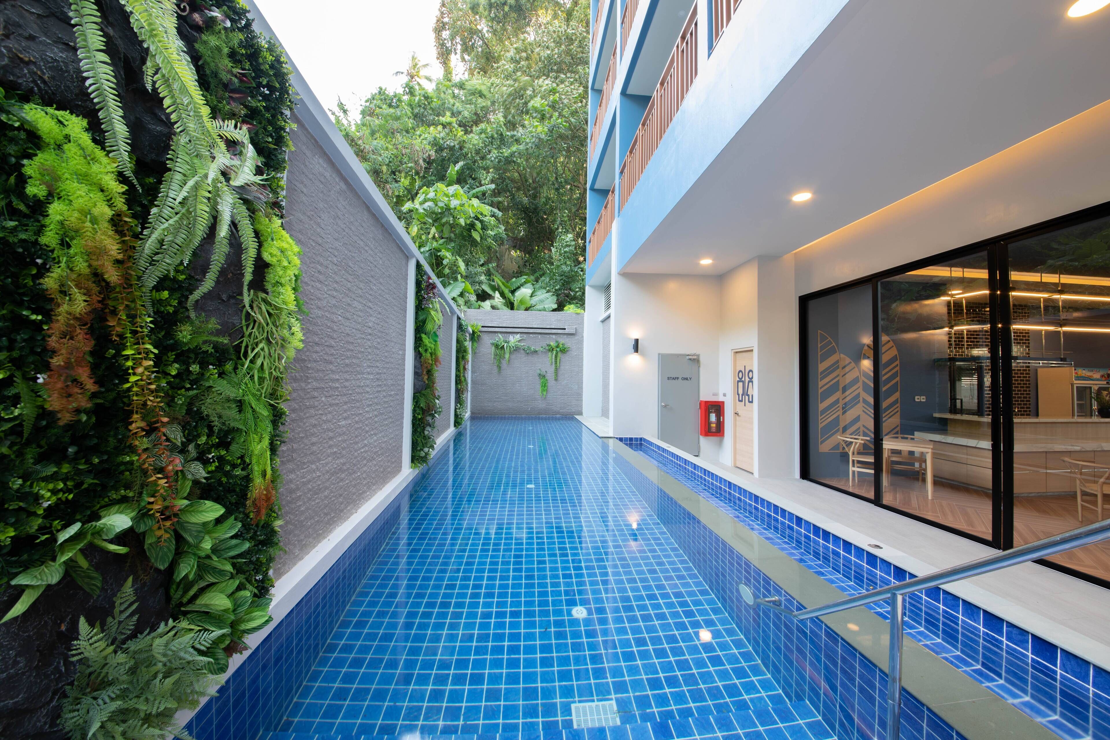 Interior de hotel moderno com piscina em azulejos azuis, plantas e área de refeições contemporânea.