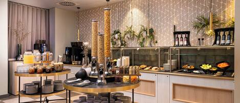 Um balcão de café da manhã moderno com diversas opções de alimentos, uma máquina de café e um arranjo de plantas decorativo.