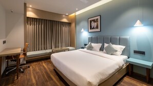 Quarto de hotel moderno com uma cama grande, uma escrivaninha, uma cadeira, um sofá e um ventilador de teto.