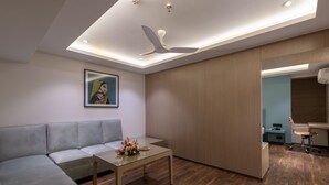 Uma sala de estar moderna com um sofá cinzento, uma mesa de centro de vidro com flores, um ventilador de teto, iluminação embutida e piso de madeira.