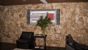 Paredes de pedra com uma obra de arte emoldurada, uma poltrona de couro preto, uma pequena mesa lateral com uma planta e um sofá preto.
