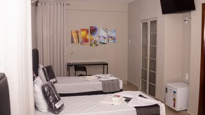 Quarto de hotel com duas camas, uma escrivaninha, uma cadeira, televisão e obras de arte na parede.
