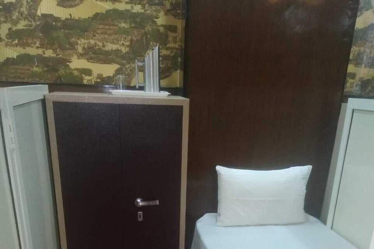 Quarto pequeno com uma cama, mesa de cabeceira, guarda-roupa e tapete vermelho.
