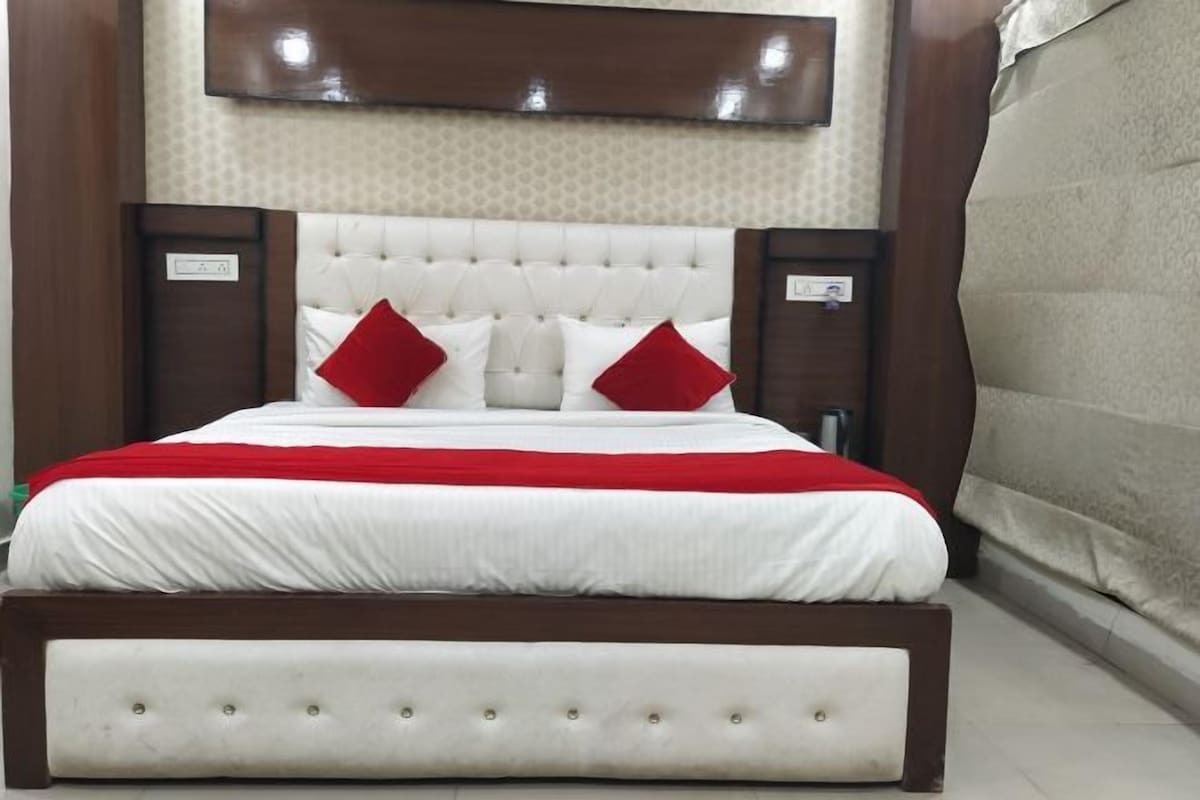 Cama bem arrumada com cabeceira branca e almofadas vermelhas, estrutura de madeira e manta vermelha.