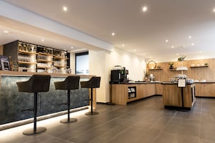 Uma área de bar moderna com banquetas, prateleiras cheias de garrafas e um espaço para café.