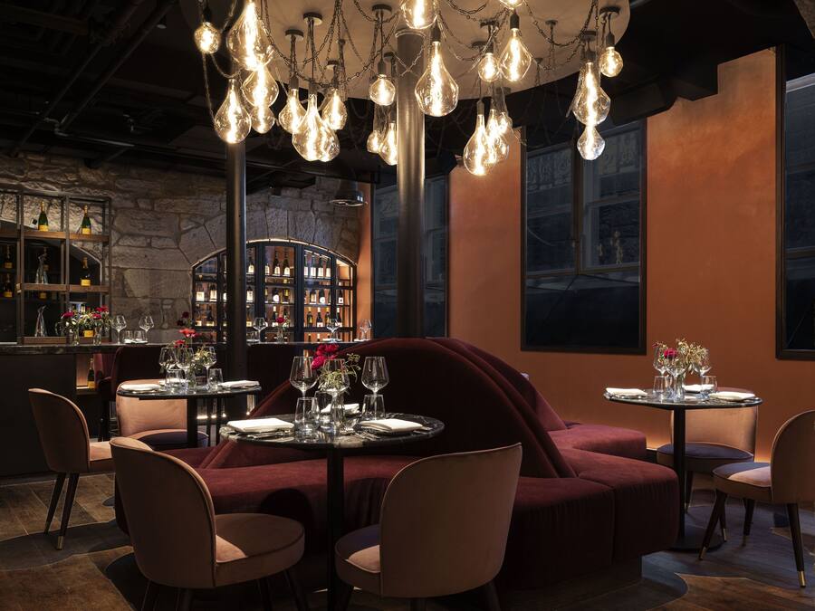 Restaurante com mesas redondas, assentos estofados vermelhos e luminárias pendentes.