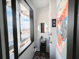 Casa de banho com uma janela grande, uma pia, um espelho e um mural colorido.