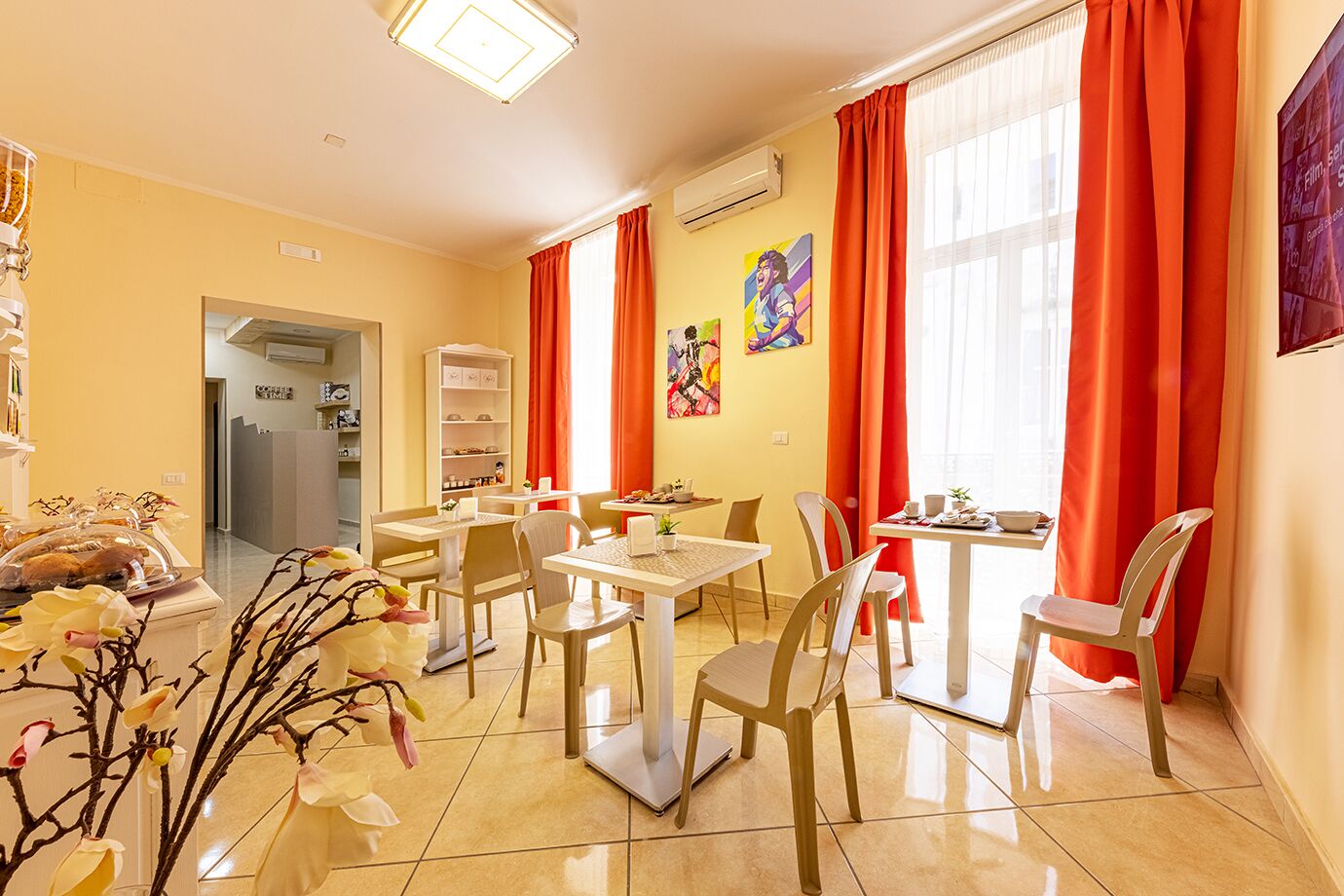 Uma sala de jantar luminosa com uma mesa e cadeiras, um buffet com comida e uma cozinha ao fundo.
