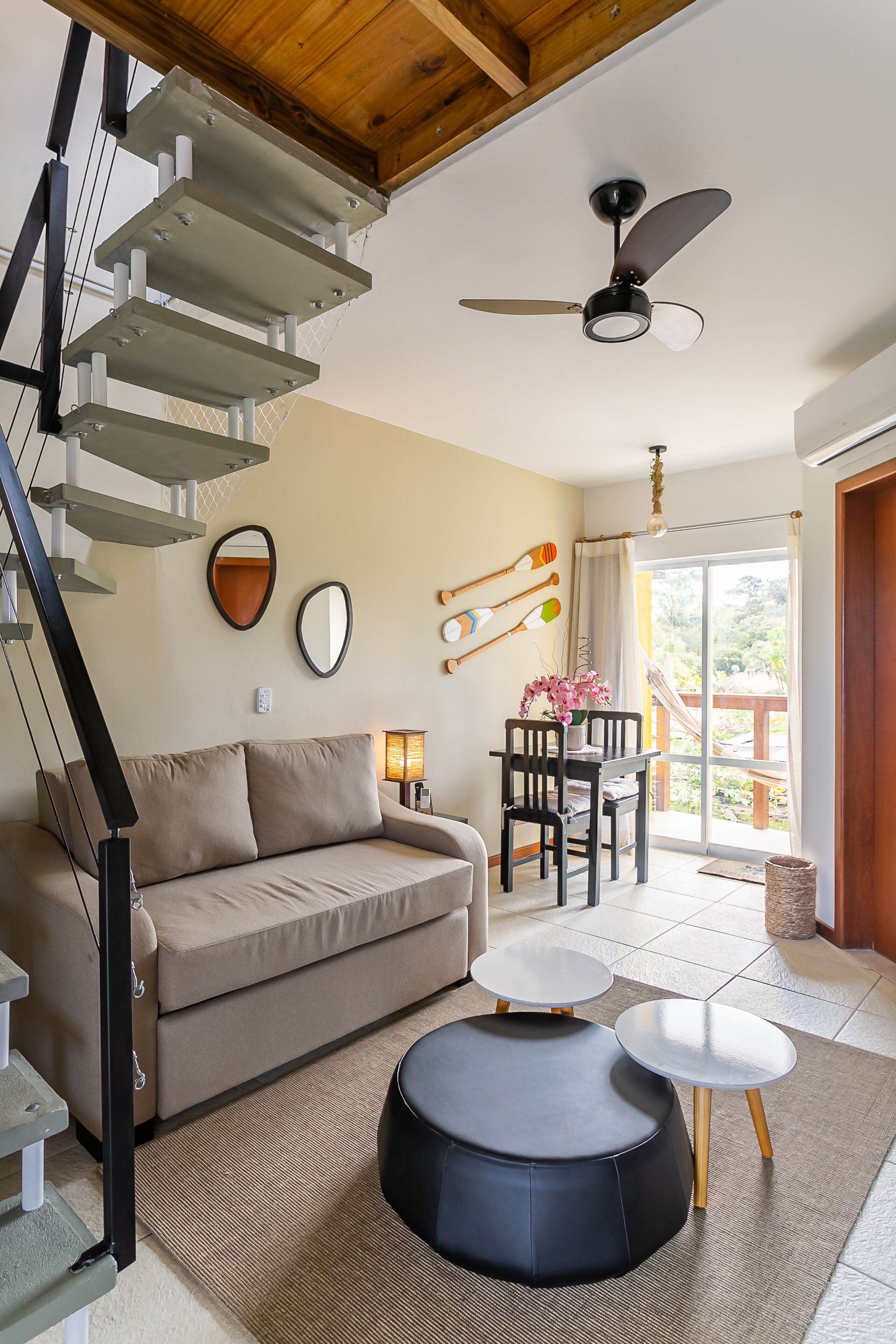 Uma sala de estar moderna com escada, ventilador de teto, sofá, mesa de centro e um espaço de jantar com cadeiras e mesa.