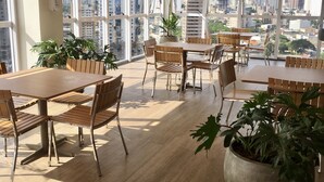 Uma área de refeições ampla, com pé direito alto e grandes janelas que proporcionam vista para a cidade.