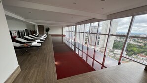 Quarto de hotel moderno com um corredor longo, um tapete vermelho e grandes janelas com vista para a cidade.