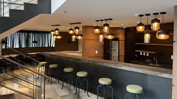 Cozinha moderna com área de bar, destacando bancada de aço inoxidável, banquetas e iluminação pendente.