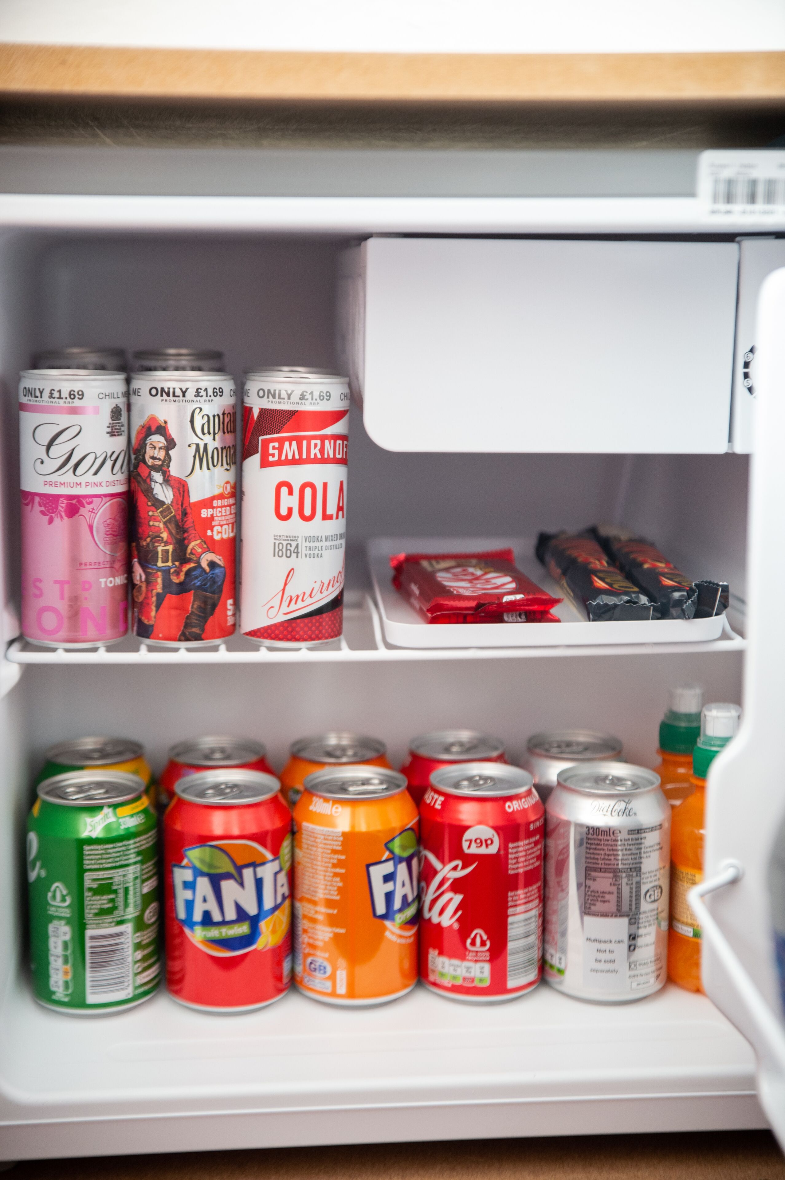 Uma geladeira repleta de diversas bebidas, incluindo Fanta, Coca-Cola e Smirnoff Cola.