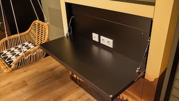 Um quarto com um banco marrom escuro, uma cadeira de vime com almofada estampada e piso de madeira.