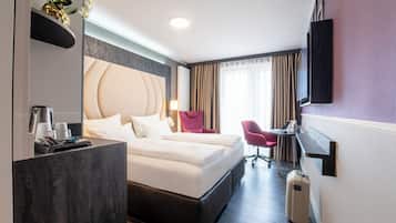 Quarto de hotel com uma cama, escrivaninha, cadeira, televisão e mala.