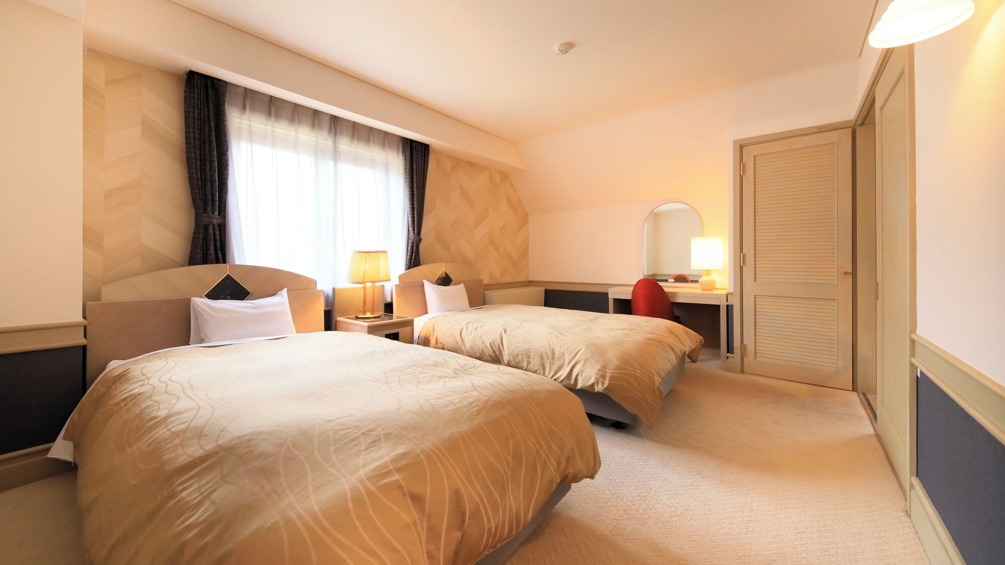 Quarto de hotel com duas camas, uma escrivaninha, uma cadeira, um espelho e um guarda-roupa.