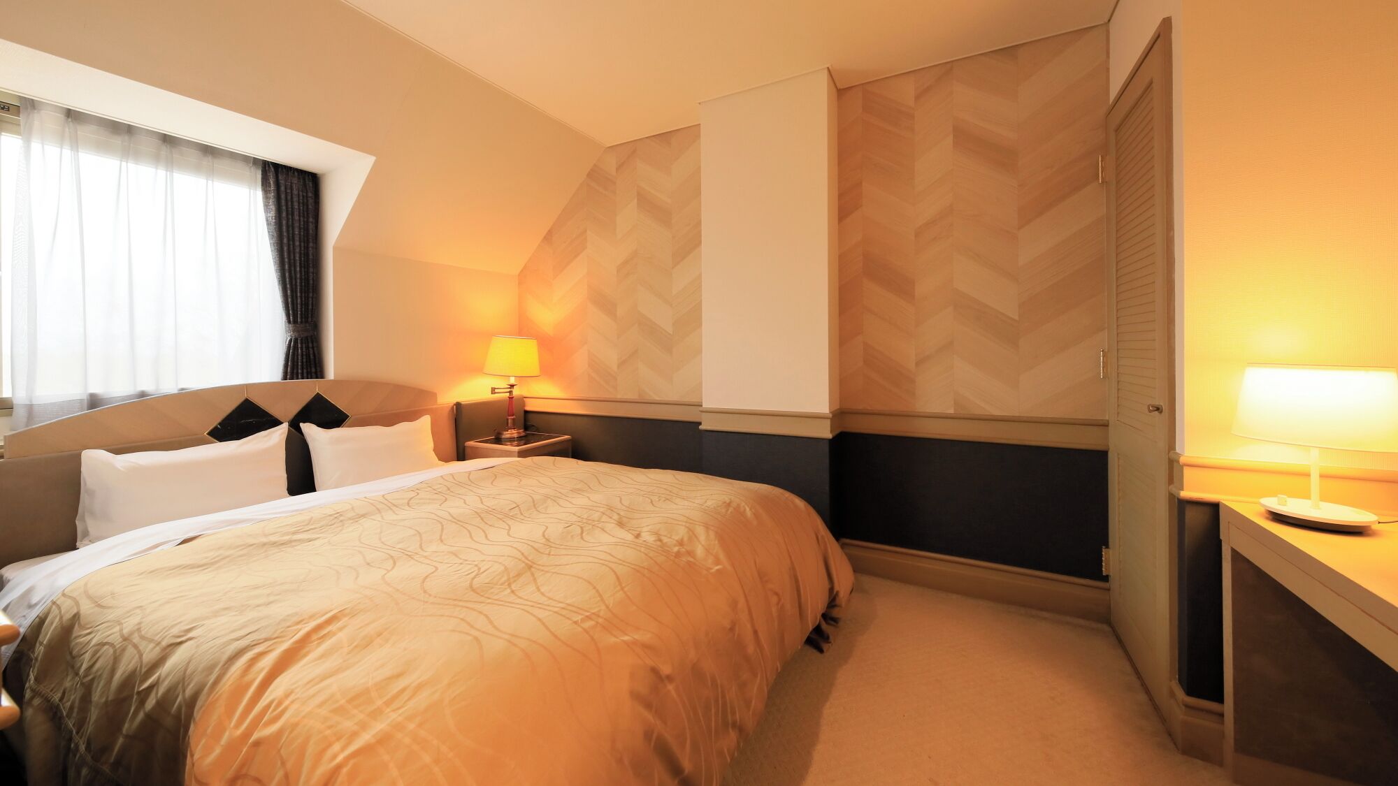 Quarto de hotel com cama, mesas de cabeceira, luminária, janela com cortinas e parede com padrão losango.