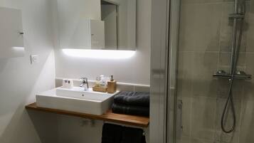 Casa de banho moderna com lavatório branco, espelho e chuveiro.