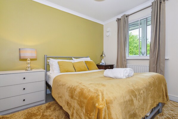 Quarto bem arrumado com cama, mesa de cabeceira, abajur e janela com cortinas.