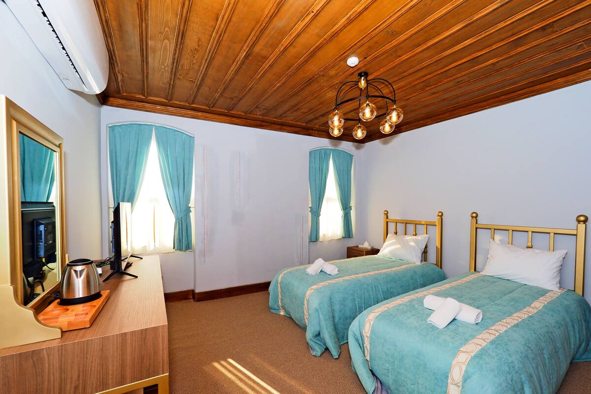 Quarto de hotel com duas camas, teto de madeira e uma mesa com chaleira.