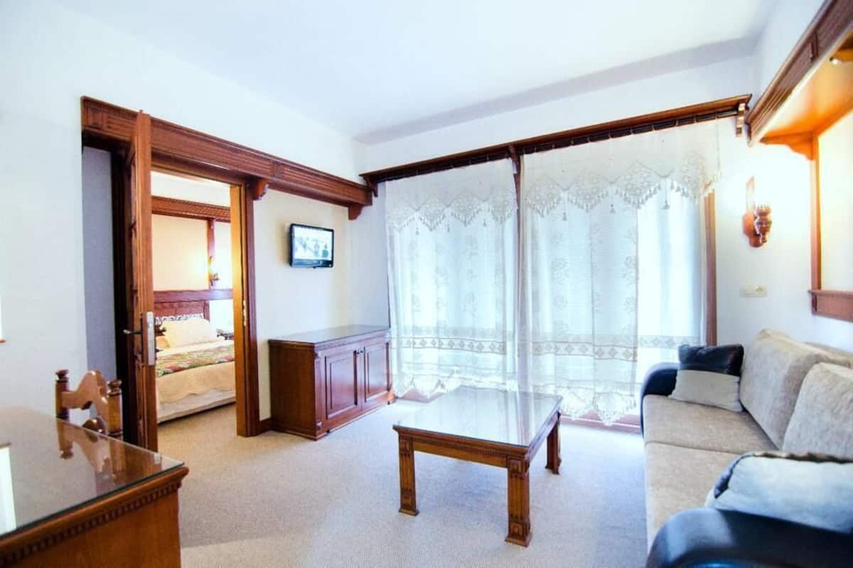 Uma sala de estar com uma mesa de madeira, um sofá, um armário e uma cama no quarto vizinho.