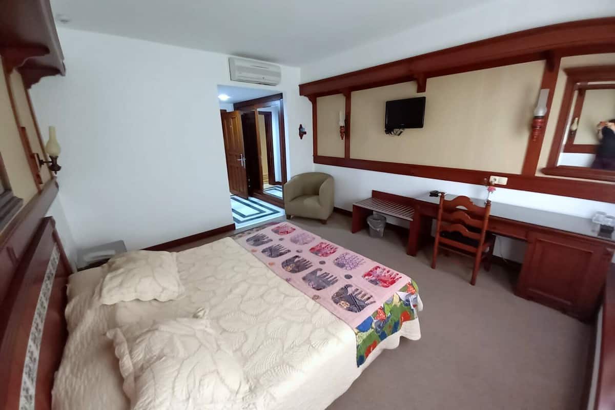 Quarto com cama, escrivaninha, cadeira, televisão e porta que dá para outro cômodo.