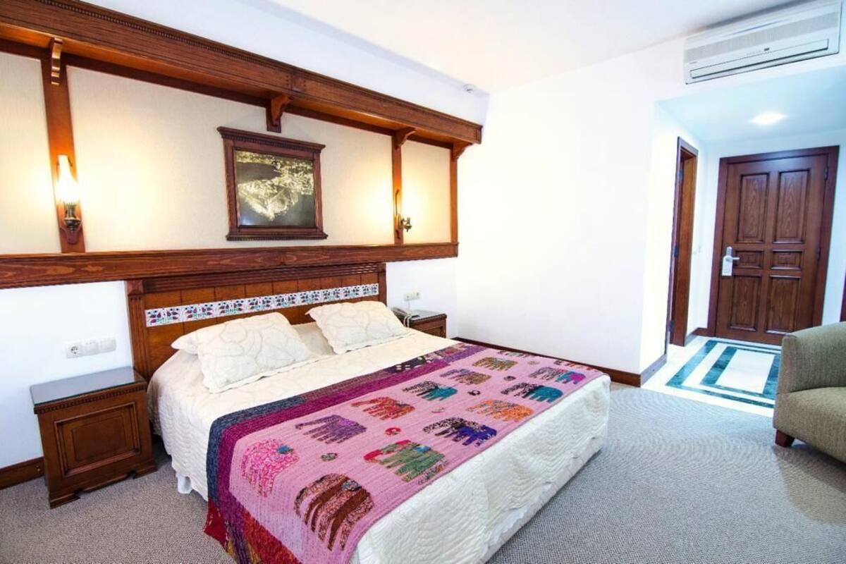 Quarto com cabeceira de madeira, cama com colcha colorida, luminárias de cabeceira e um quadro na parede.