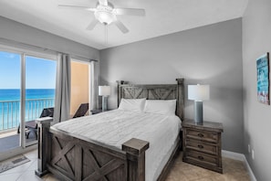 Quarto com uma cama grande, duas mesas de cabeceira, ventilador de teto e vista para o mar.