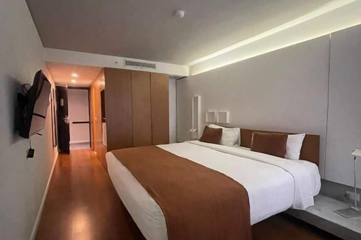 Quarto de hotel moderno com uma cama grande, televisão de tela plana na parede e um closet espaçoso.