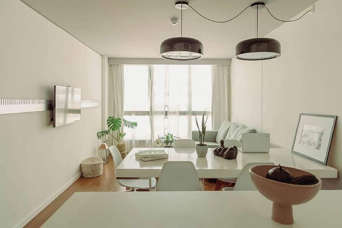 Sala de estar moderna com área de jantar, incluindo um sofá, uma mesa de centro e uma TV fixada na parede.